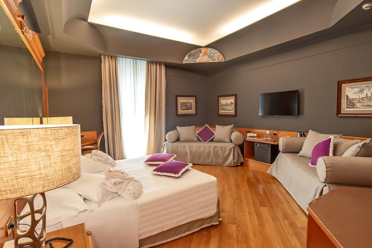Quarto de hotel com uma cama, dois sofás, uma mesa e uma televisão.