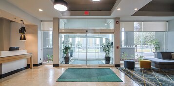 Um saguão de hotel com balcão de recepção, um tapete verde, um sofá e uma grande porta de vidro que dá para o exterior.
