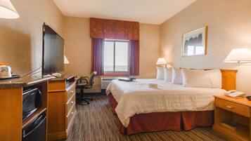 Quarto de hotel com cama, escrivaninha, televisão e janela com cortinas.