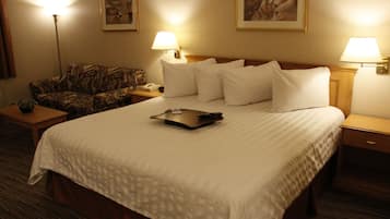 Quarto de hotel com uma cama grande, duas mesas de cabeceira, uma luminária, um telefone e um sofá com padrão floral.