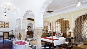 Um quarto de hotel luxuoso com uma cama grande, um espaço de estar, uma banheira com pétalas de rosa e decoração requintada.