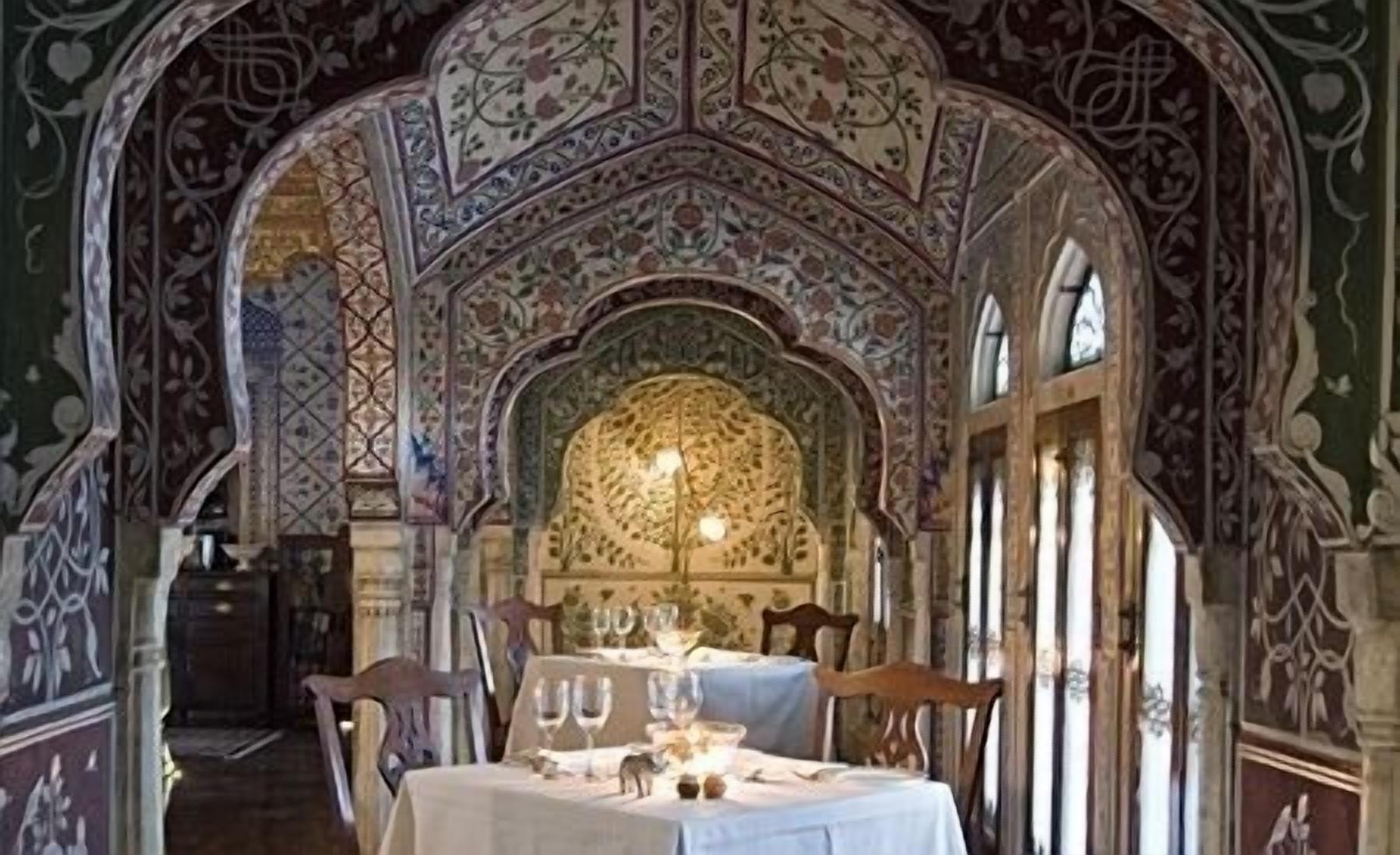 Uma elegante sala de jantar com detalhes elaborados no teto, uma mesa posta para dois e vista para o interior do edifício.