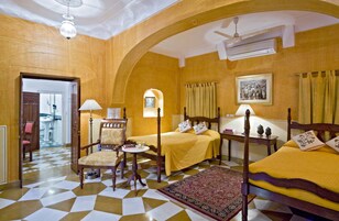 Quarto de hotel com duas camas, área de estar com uma cadeira e mesa, tapete estampado e um espelho grande.