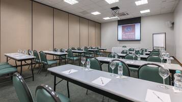 Uma sala de conferências com mesas, cadeiras, garrafas de água e uma tela de apresentação exibindo "Comfort Suites".