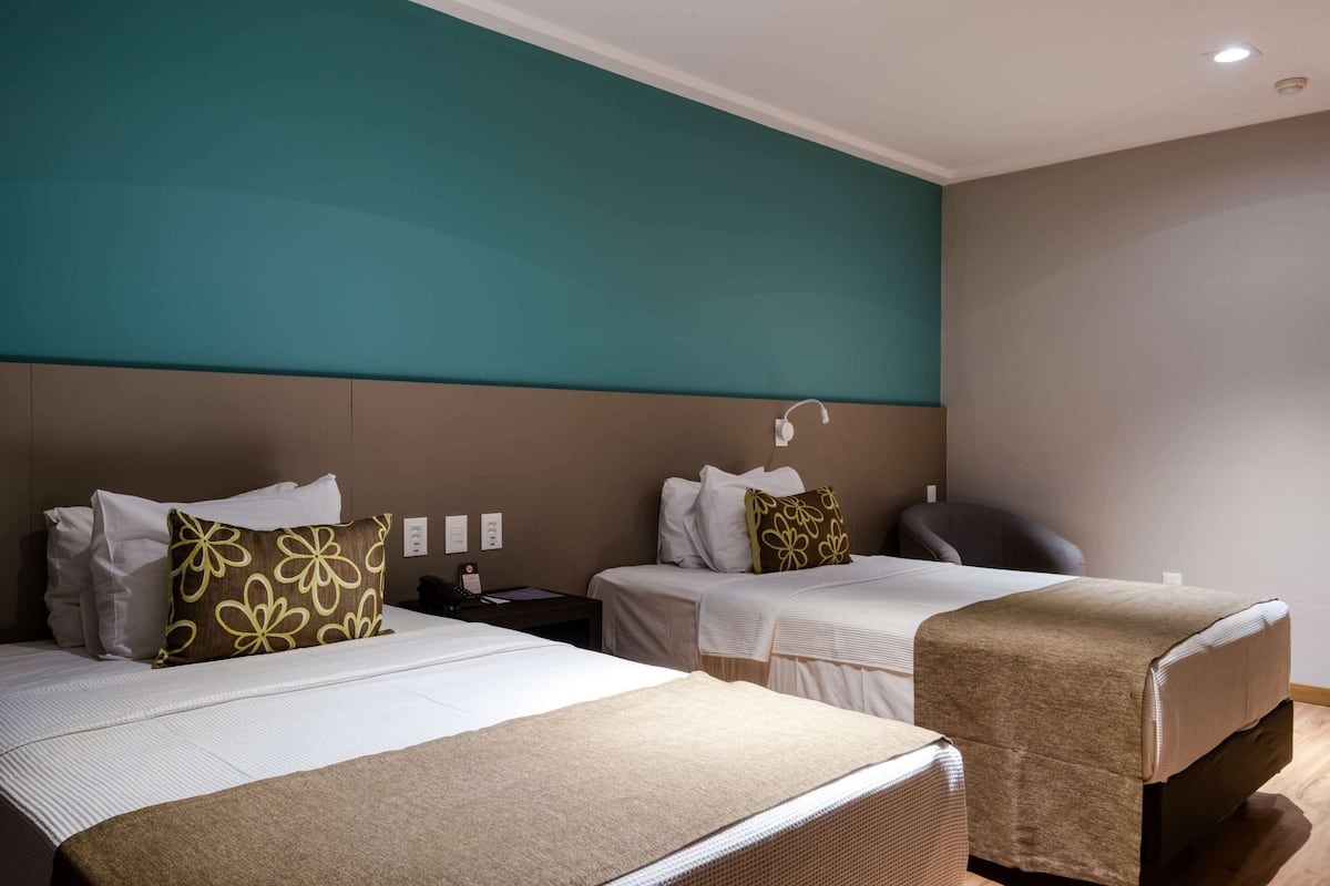 Quarto de hotel com duas camas, uma escrivaninha e uma cadeira.