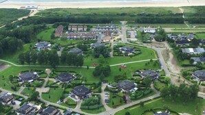 Vista aérea de uma área residencial com casas, um edifício central e uma praia ao fundo.