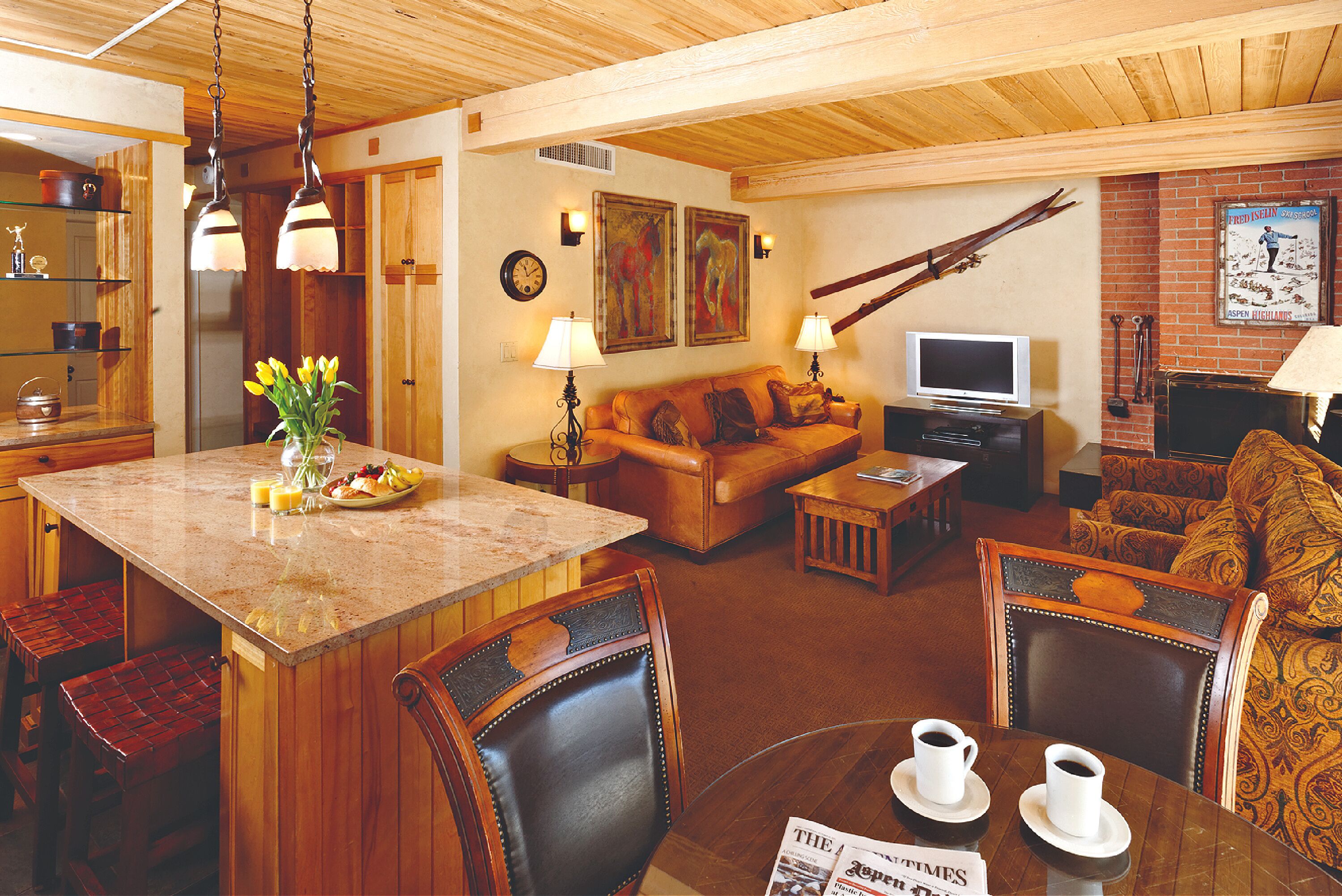 Uma sala de estar acolhedora com teto de madeira, lareira, televisão e mesa de jantar com cadeiras.