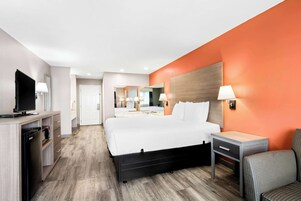 Quarto de hotel com cama, mesa de cabeceira, abajur e televisão sobre um suporte.