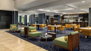 Um lobby de hotel moderno com sofás verdes, cadeiras amarelas, uma área de bar e um espaço de estar com mesas e cadeiras.