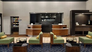 Um lobby moderno com uma mesa de recepção, área de estar e uma pequena copa.