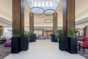 Um hall amplo com pé-direito alto, luminárias modernas e plantas em vasos.