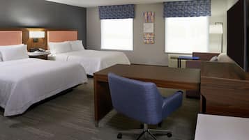 Quarto de hotel com duas camas, uma escrivaninha, uma cadeira, televisão e obras de arte nas paredes.