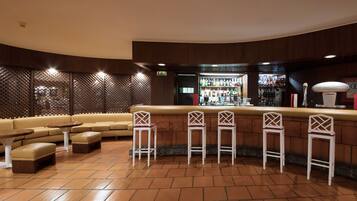Uma área de bar com balcão curvo, vários bancos e um espaço de estar com sofá e apoio para os pés.
