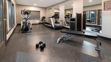 Uma academia com equipamentos de exercícios, um banco e halteres.