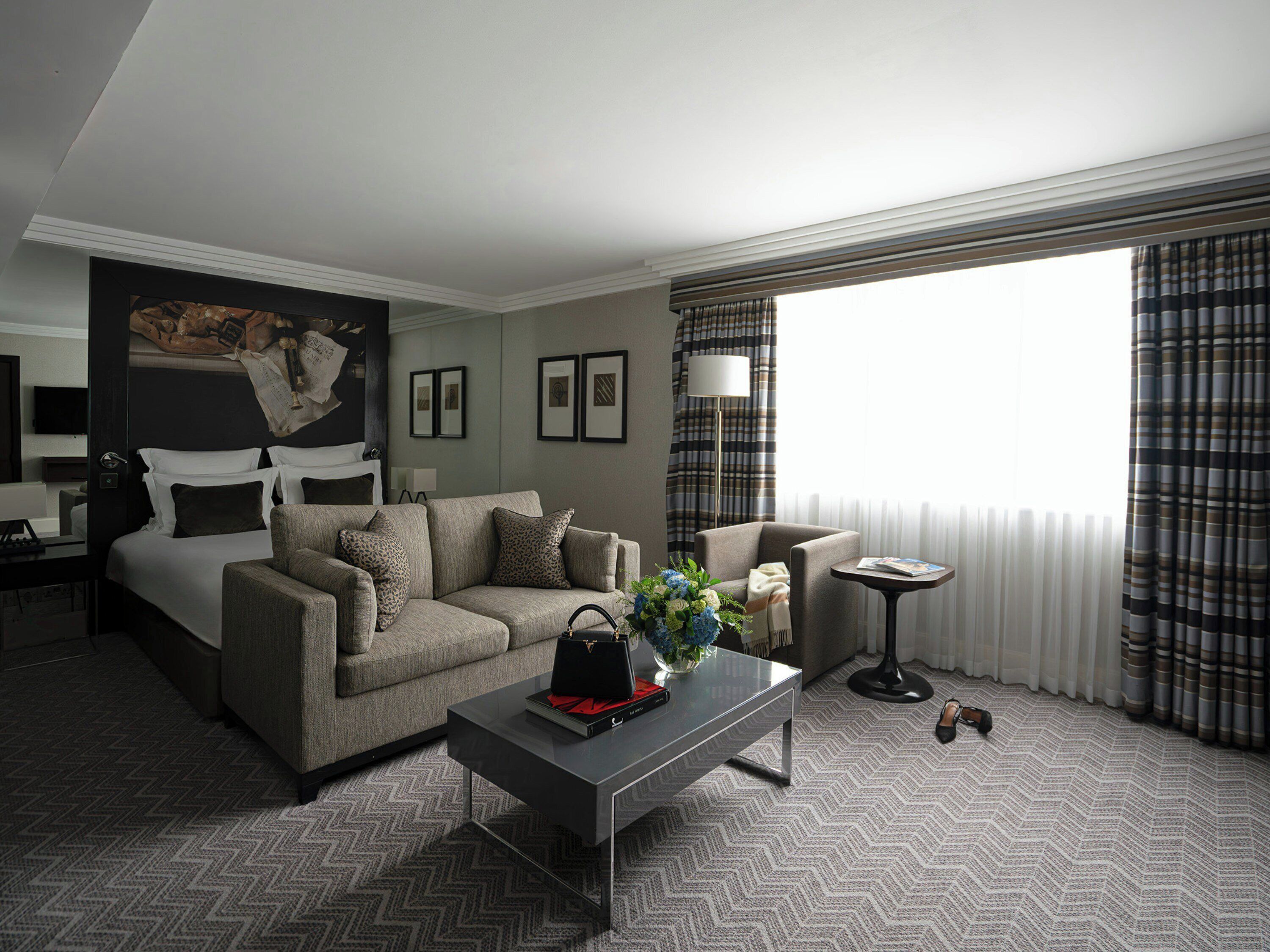 Quarto de hotel com cama, sofá, mesa de centro e mesinha de cabeceira.