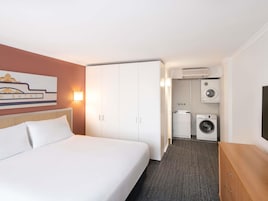 Quarto de hotel com cama, guarda-roupa, máquina de lavar e televisão presa na parede.