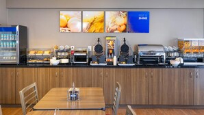 Um balcão de café da manhã com diversos alimentos e eletrodomésticos, incluindo uma máquina de café e uma máquina de waffle.