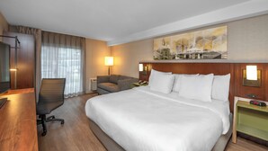 Quarto de hotel com uma cama grande, uma escrivaninha com cadeira, uma televisão e um quadro na parede.