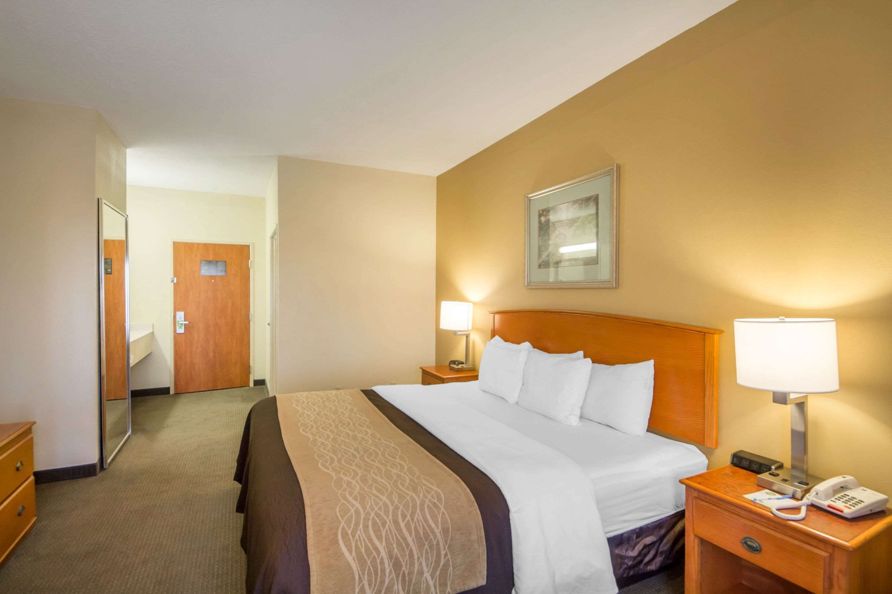 Quarto de hotel com cama, mesas de cabeceira, abajur, telefone e porta.