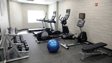 Ginásio com esteiras, elípticas, halteres e uma bola de exercícios azul.