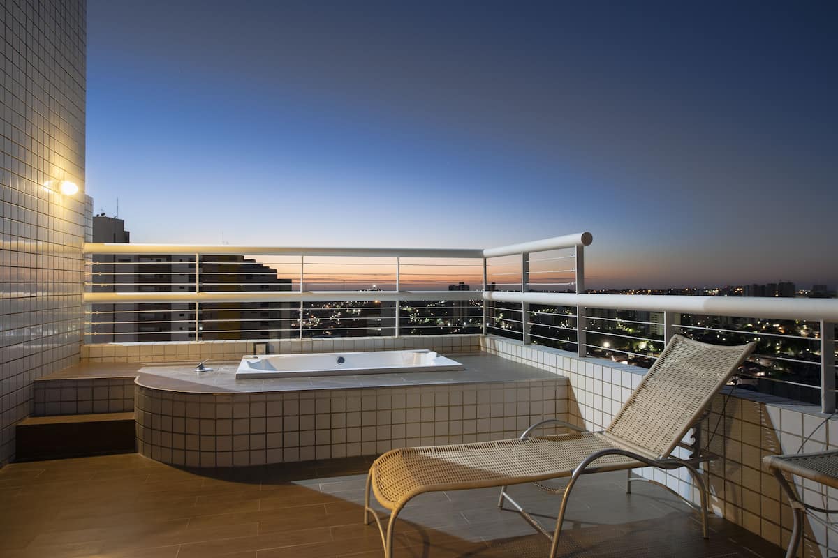 Terraço no telhado com hidromassagem e cadeiras de vime, com vista para a cidade ao entardecer.