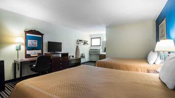 Quarto de hotel com duas camas, uma secretária com computador, televisão e uma janela.