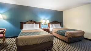 Quarto de hotel com duas camas, uma mesinha de cabeceira, um abajur e uma cadeira.
