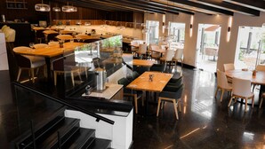 Um restaurante moderno com divisória de vidro, mesas de madeira e chão com ladrilhos pretos.