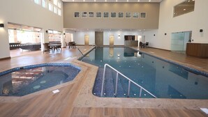 Piscina interior com chão de azulejo, uma pequena banheira de hidromassagem e área de recepção com balcão e cadeiras.
