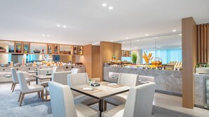 Um lobby de hotel moderno com um balcão de recepção de mármore, área de estar com cadeiras confortáveis e um buffet com diversas opções de comida.