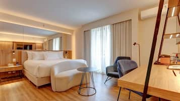Quarto de hotel com uma cama grande, uma escrivaninha, uma cadeira, uma mesinha e um espelho.