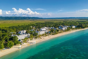 Vista aérea de um resort costeiro com villas na praia, uma praia de areia e mar azul cristalino.