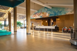 Um hall amplo com uma mesa de recepção, áreas de estar e um grande mural na parede.