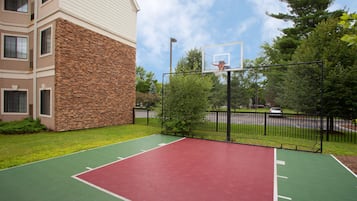 Quadra de basquete ao ar livre, junto a um edifício com fachada de pedra.