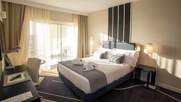 Quarto de hotel com uma cama grande, uma escrivaninha com um laptop, uma cadeira e vista para o exterior por uma porta de correr.