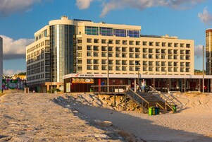 Um hotel com um clube de praia, várias varandas e uma escadaria que dá para a praia.