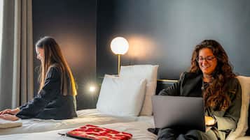Quarto de hotel com duas camas, uma luminária de cabeceira e um laptop sobre uma das camas.