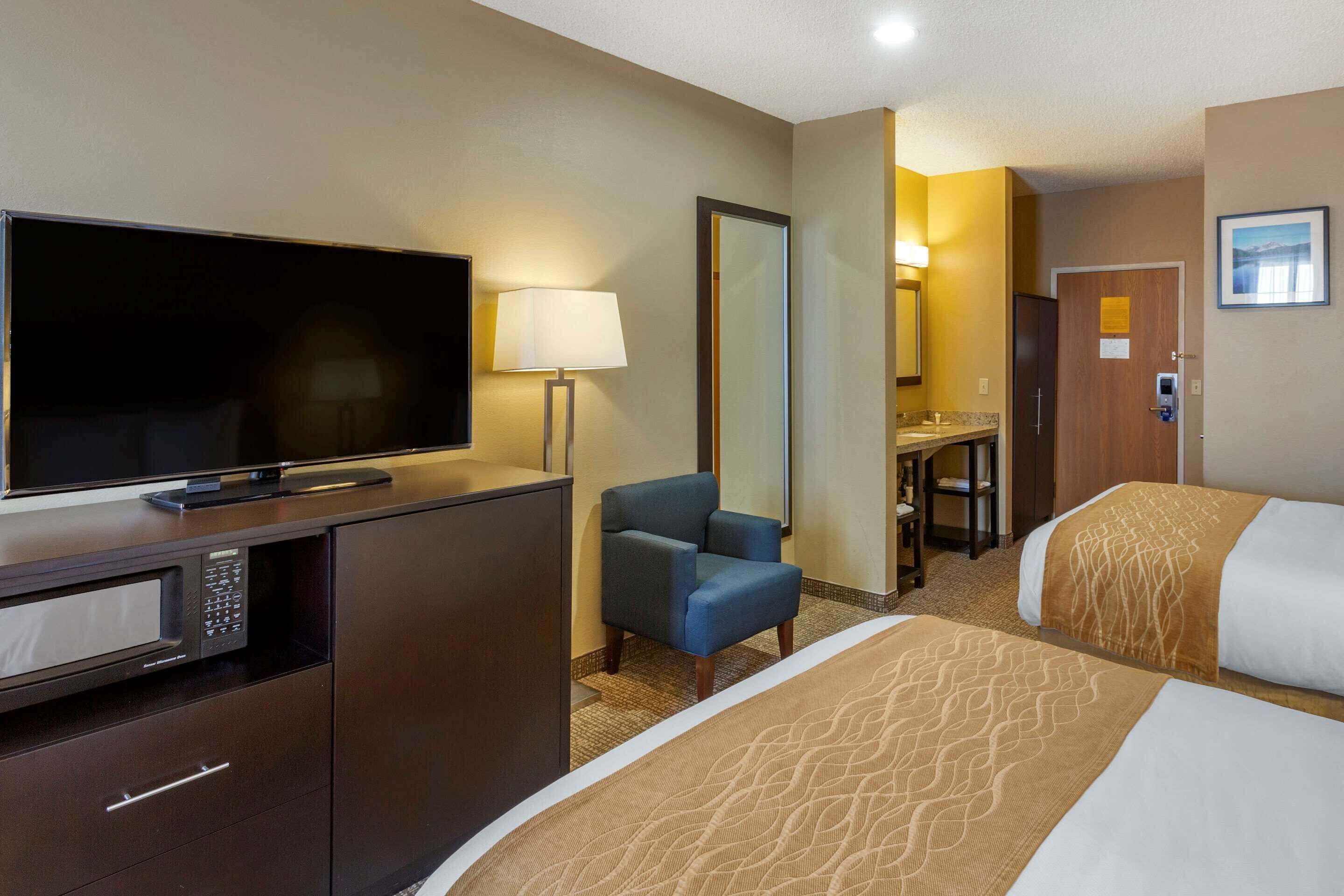 Quarto de hotel com televisão, secretária, cadeira e duas camas.