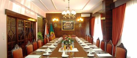 Uma sala de conferência com uma mesa comprida, cadeiras, um candelabro e uma bandeira.