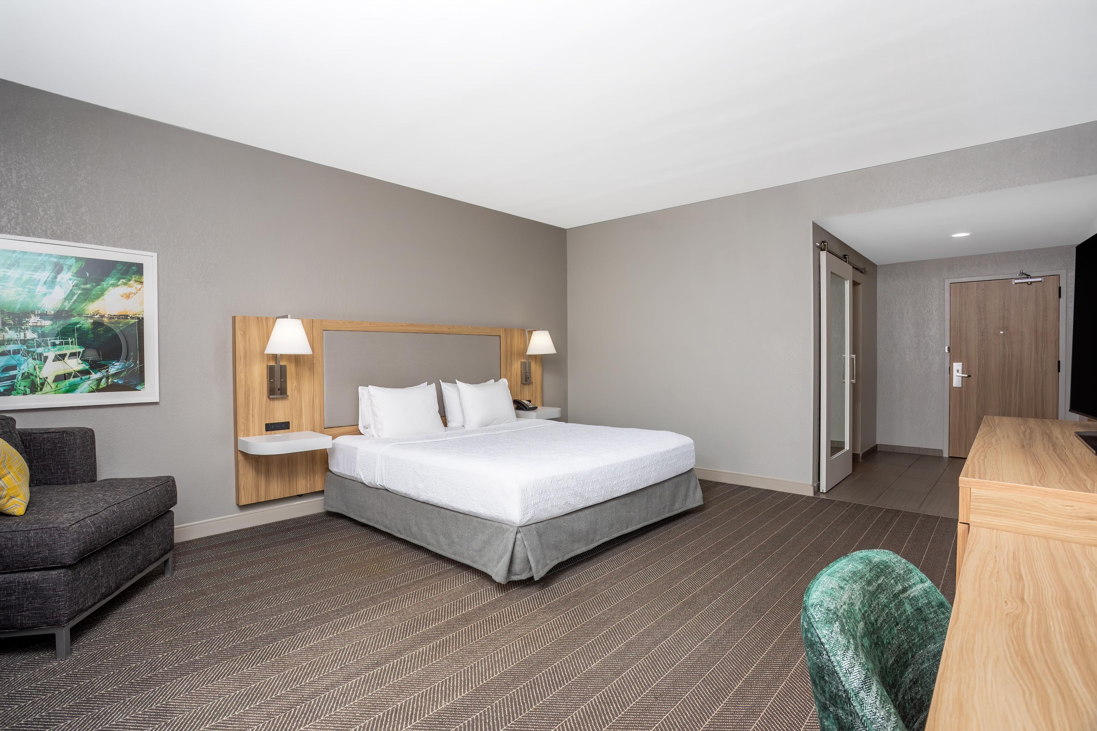 Quarto de hotel com cama, mesas de cabeceira, escrivaninha, cadeira e um quadro na parede.