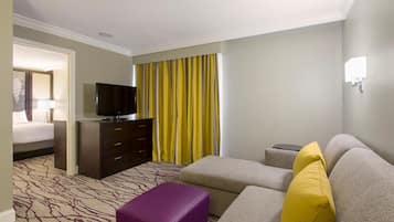 Quarto de hotel com cama, televisão, sofá, mesa pequena e mala.
