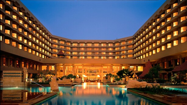 Um hotel com uma piscina grande central, várias varandas e fachada bem iluminada.