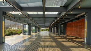 Uma passarela coberta com piso de madeira, vigas de metal e luminárias penduradas.
