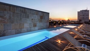 Piscina no terraço com muro de pedra e espreguiçadeiras.