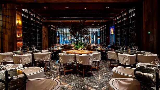 Restaurante com balcão central, diversas mesas com cadeiras e piso com padrão herringbone.