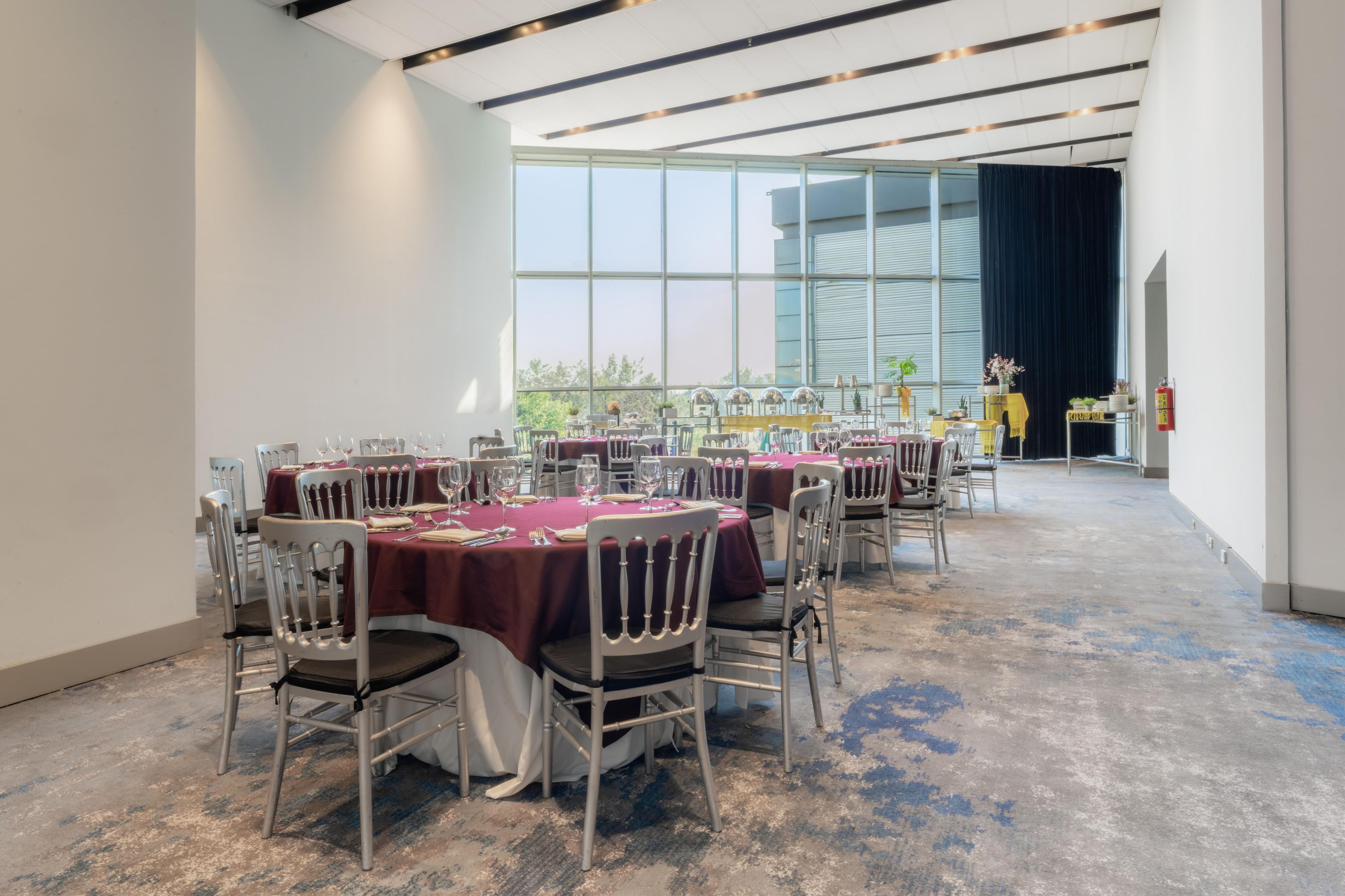 Sala de conferência com mesas preparadas para uma reunião, grandes janelas e extintor de incêndio na parede.