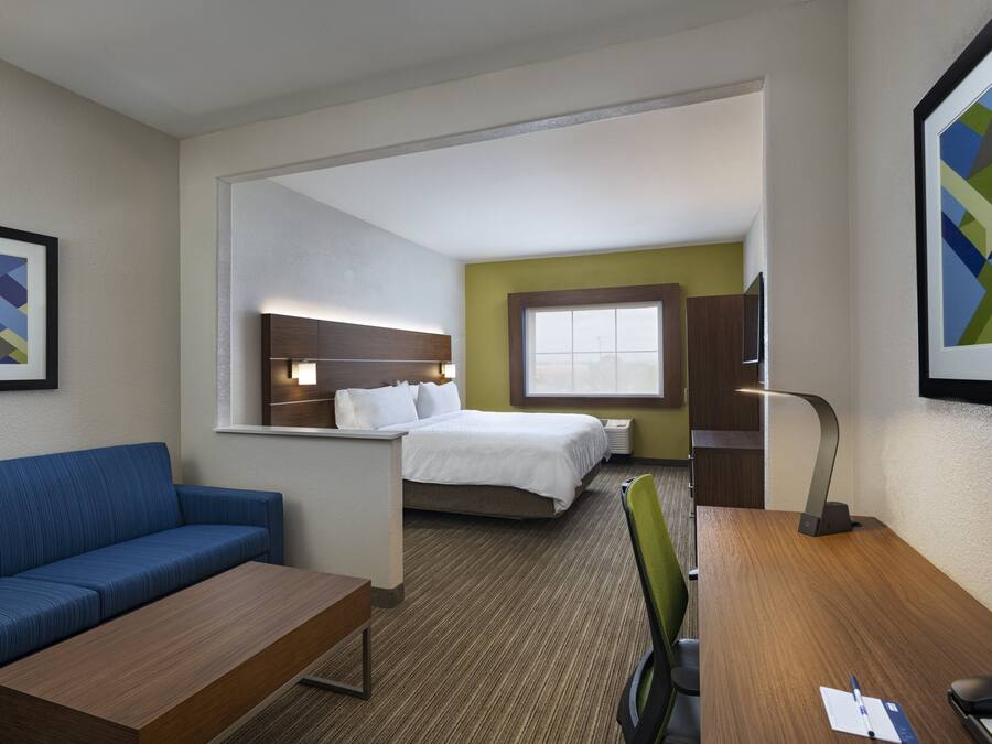 Quarto de hotel com cama, escrivaninha, cadeira, sofá e janela.