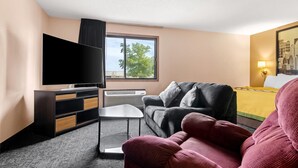 Quarto de hotel com televisão de tela plana, sofá, mesa pequena e janela com vista para a cidade.