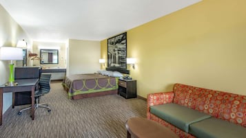 Quarto de hotel com cama, escrivaninha com cadeira, sofá e mesa pequena.