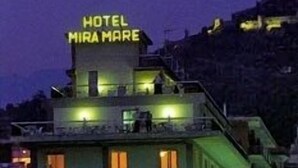 Um hotel chamado "HOTEL MIRA MARE", com várias janelas e uma placa no telhado.